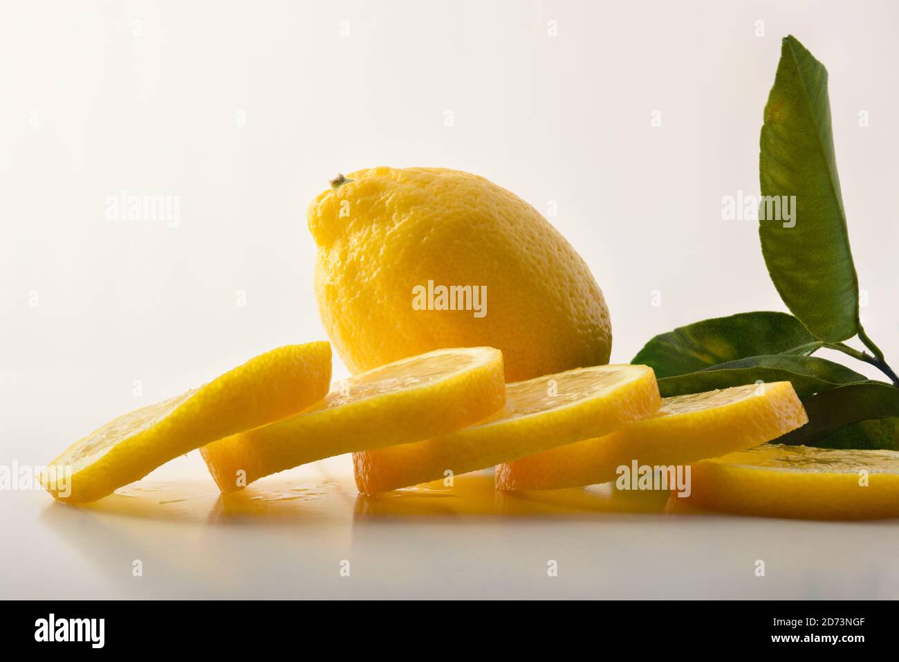 Detail of lemon cut into slices on a white table and lemon with leaves ...