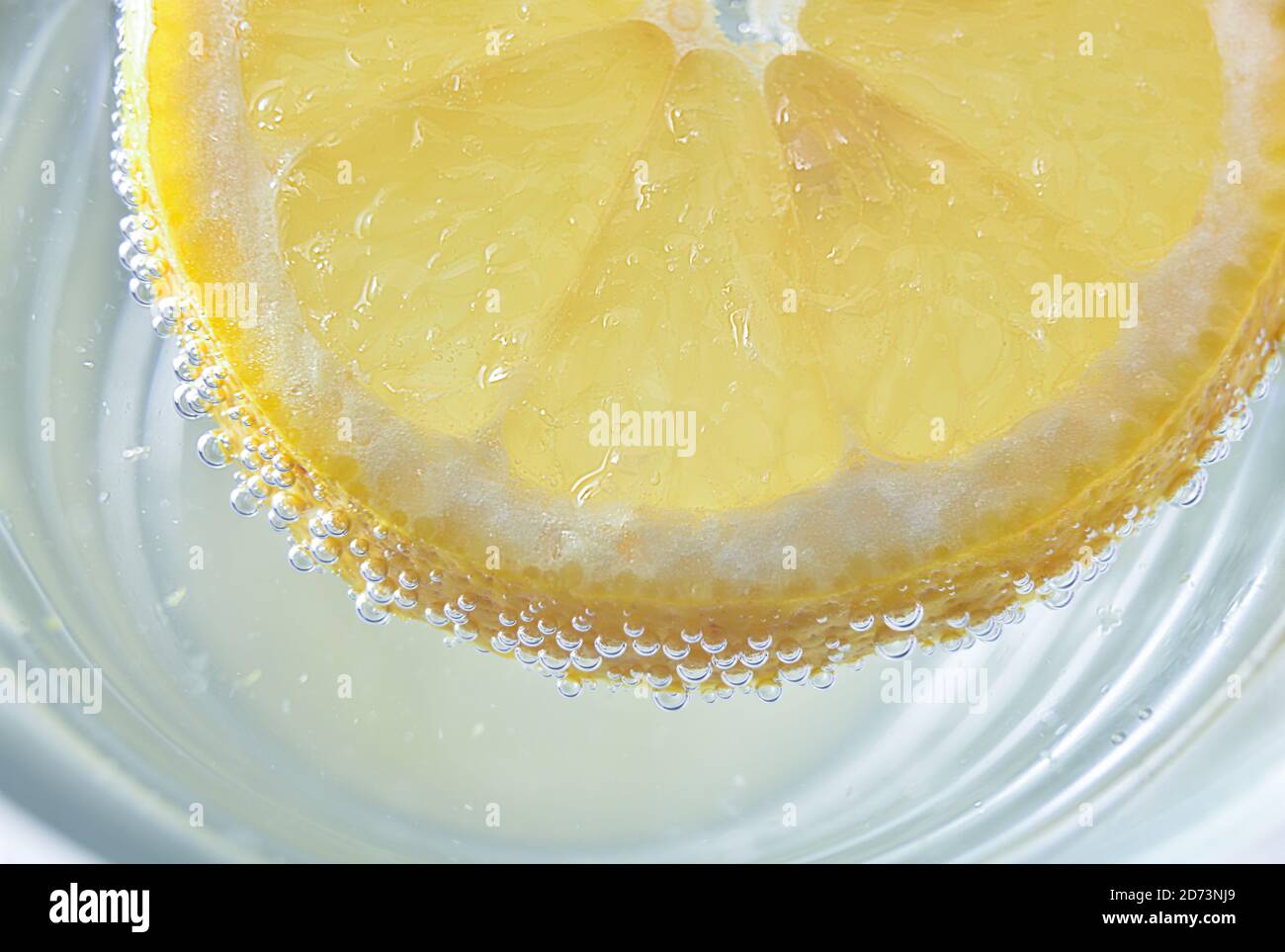 Detail of lemon slice with bubbles floating on water in a glass. Top ...