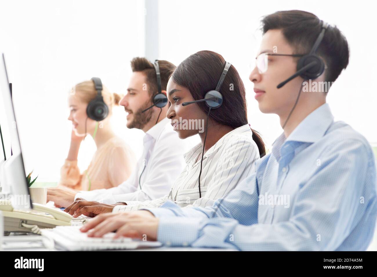 Line of call centre representatives with headsets working on computers ...