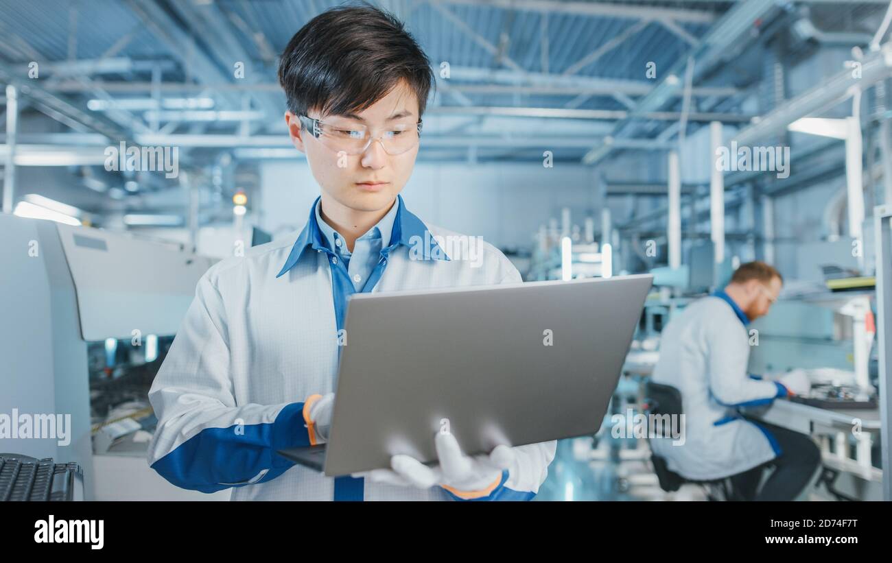 On High-Tech Factory Asian Engineer Uses Laptop Computer for Programing ...