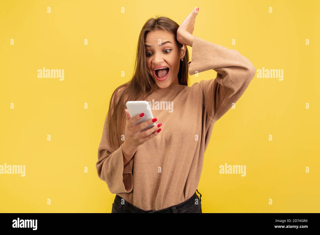 Shocked scrolling phone. Portrait of young caucasian woman on yellow ...
