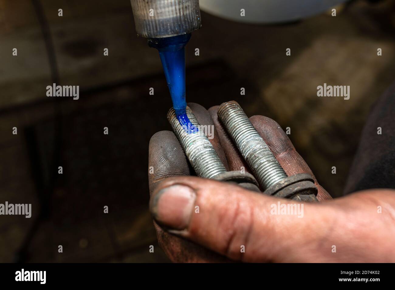 Car mechanic applies a layer of blue thread glue to the screw in his ...