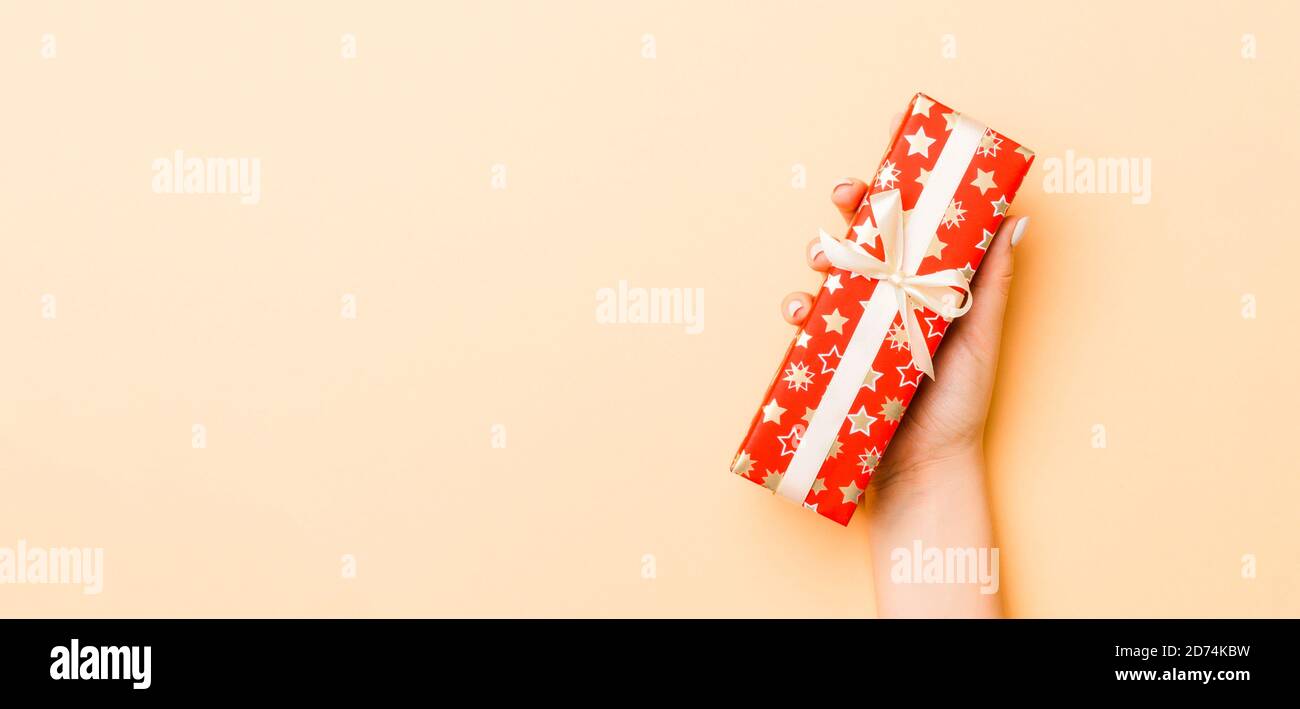 Flat lay of woman hands holding gift wrapped and decorated with bow on ...
