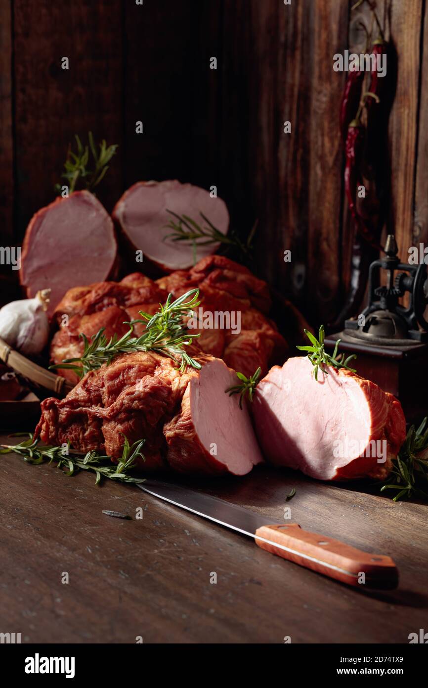 Smoked ham with herbs, spices, and kitchen utensils on an old wooden ...