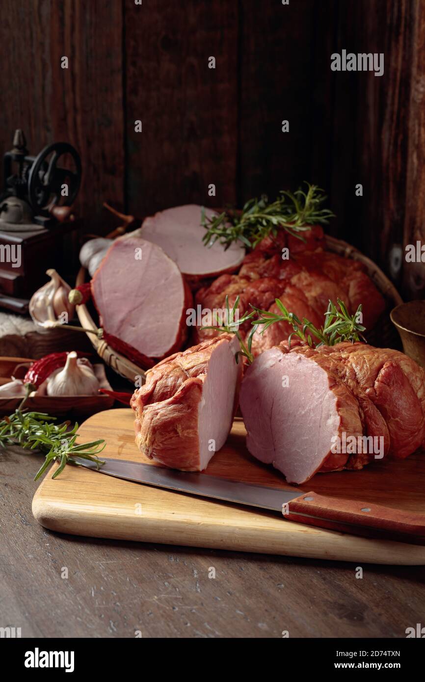 Smoked ham with herbs, spices, and kitchen utensils on an old wooden ...