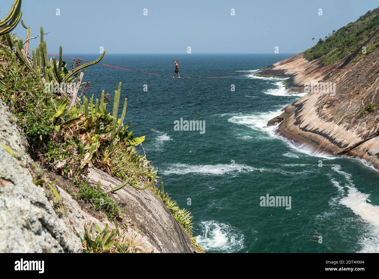 Beautiful view to highliner walking the line on rocky ocean front ...
