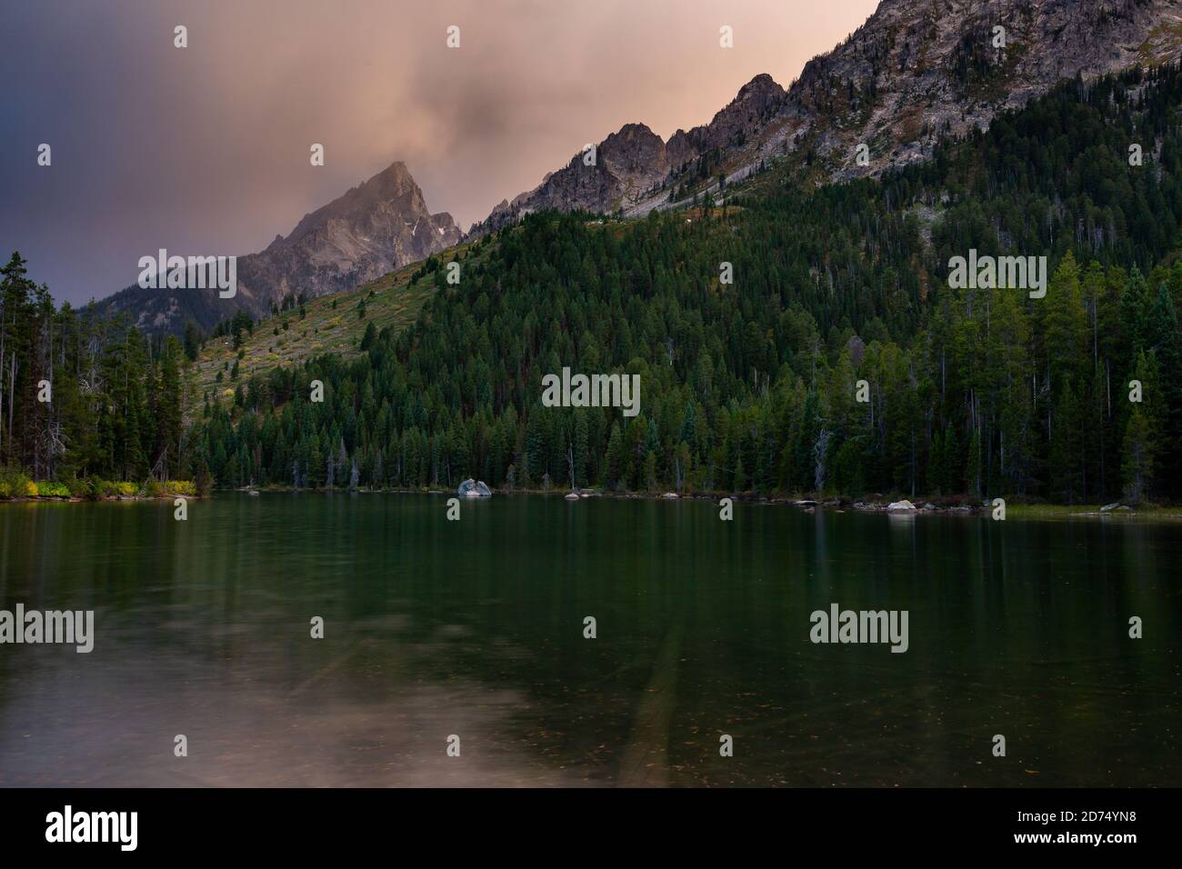 The calm waters of String Lake reflecting a colorful sunset above the ...