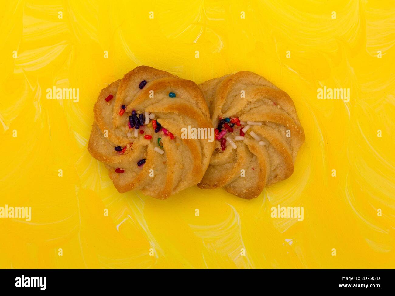 Two shortbread cookies with sprinkles on a bright yellow background ...