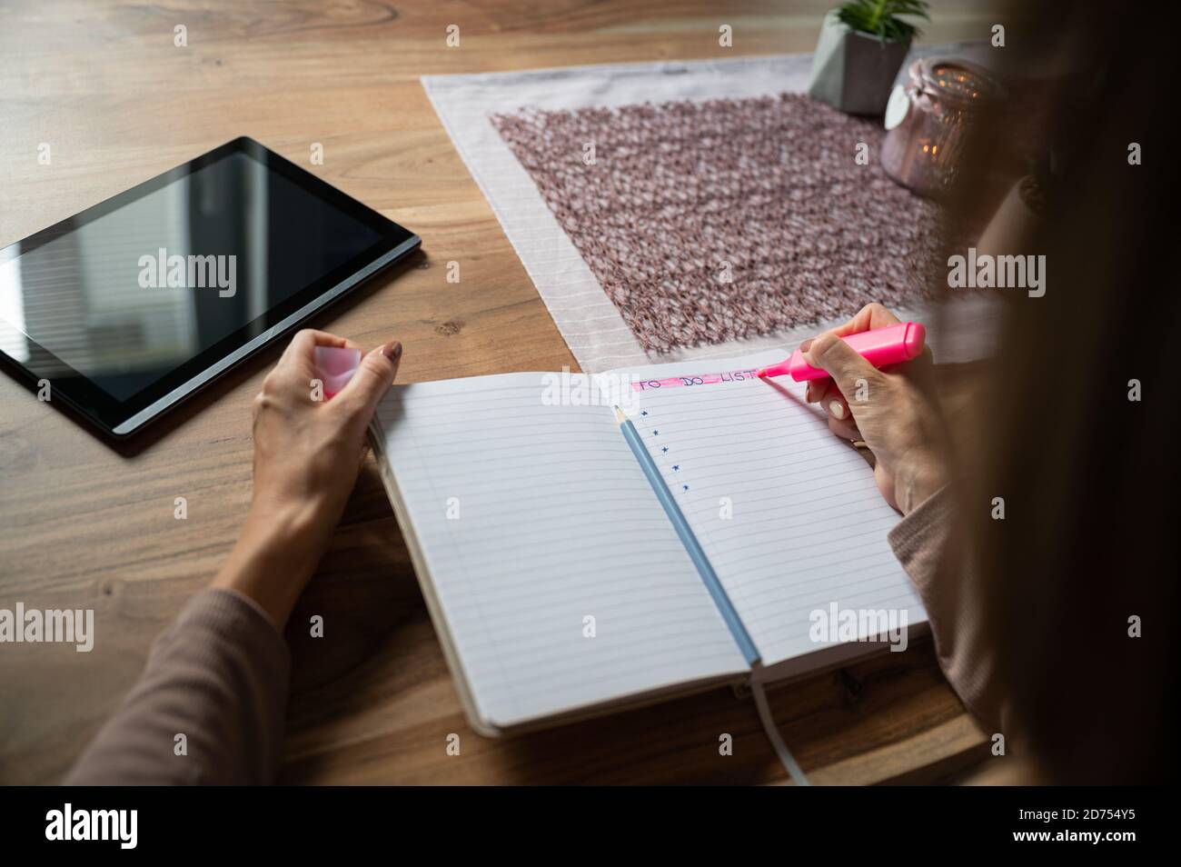Over the shoulder view of a woman writing a to do list in her notepad ...