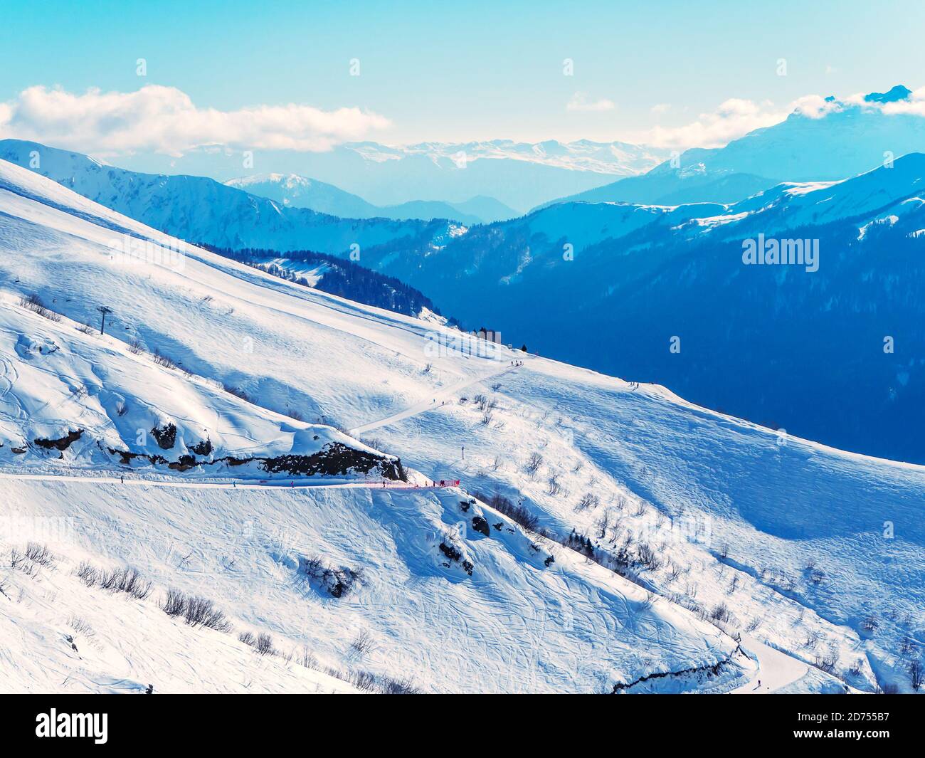 Snowy ski slopes in the background of mountain ranges and blue sky with ...