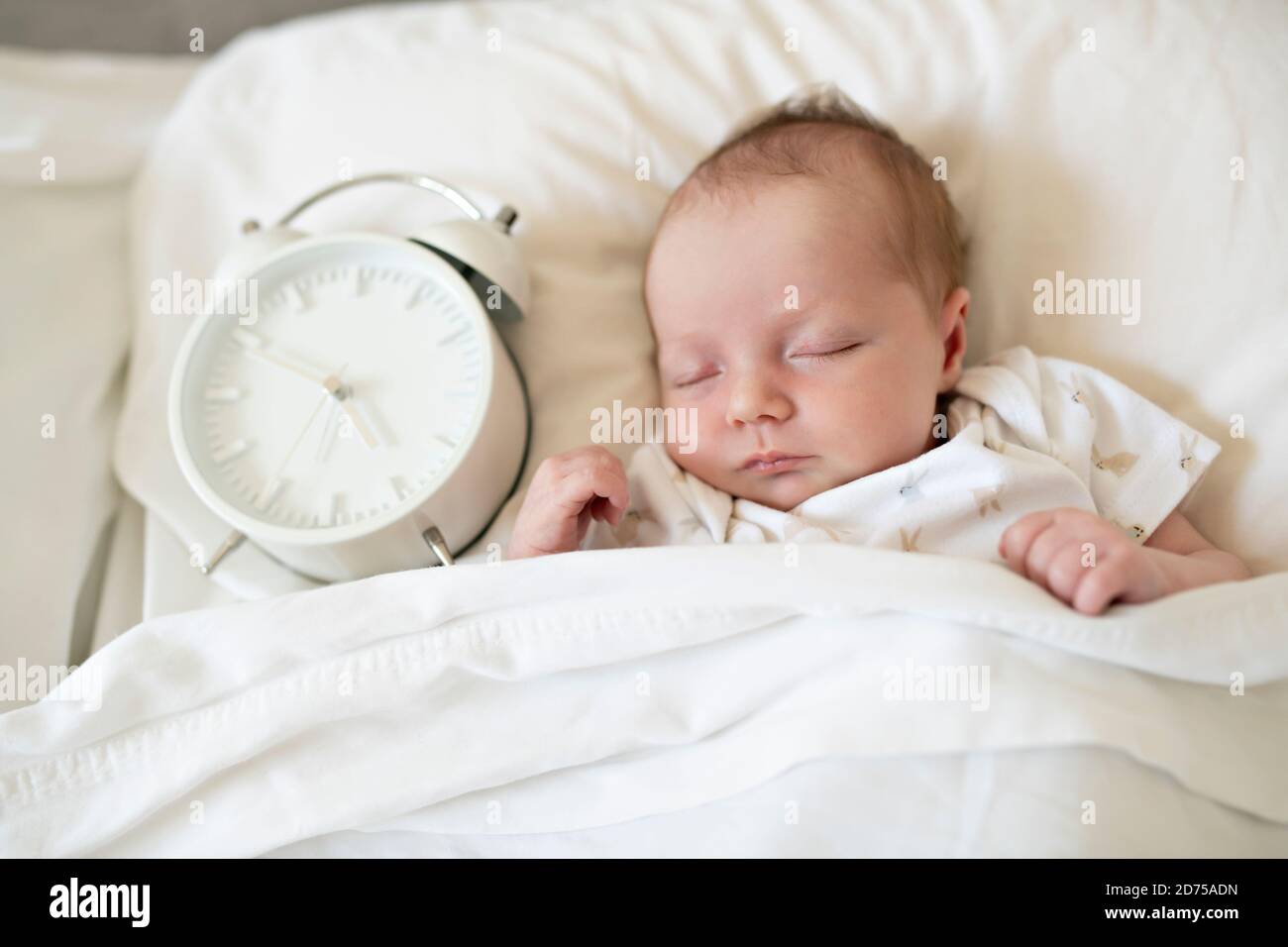 A Sweet newborn baby girl sleeping in white bed with clock on the side Stock Photo - Alamy