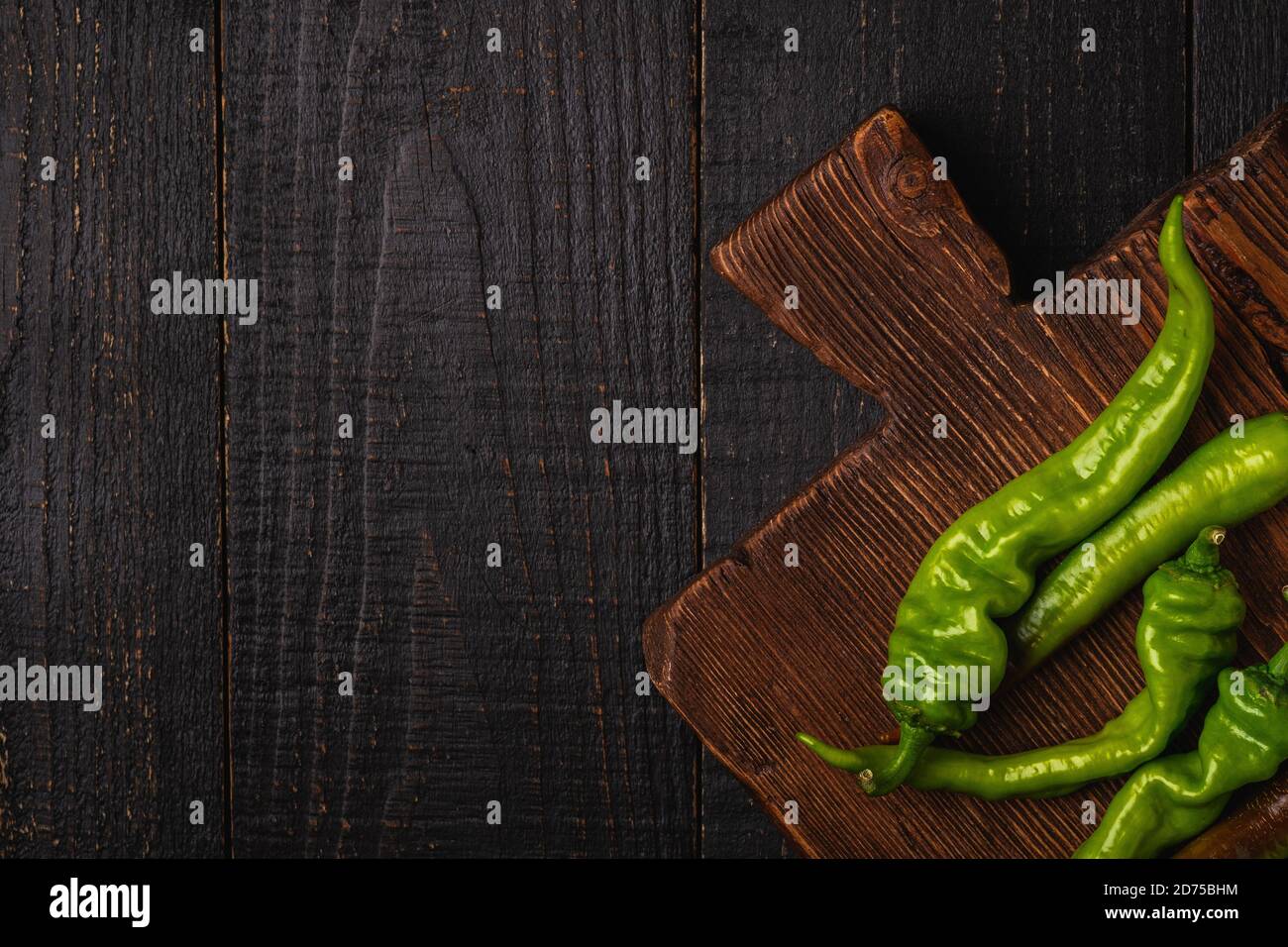 Hot spicy green chili peppers on teak wooden cutting board, dark wood ...
