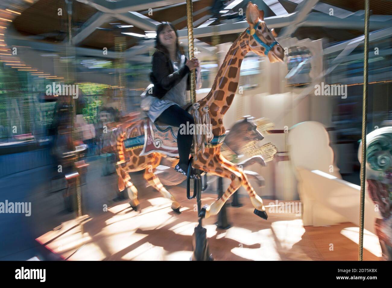 A young Asian girl riding a giraffe on a carousel or merry go round in ...