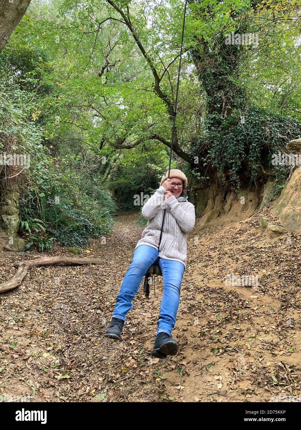 Woman swinging on a rope swing hanging from a tree in a hollow way ...