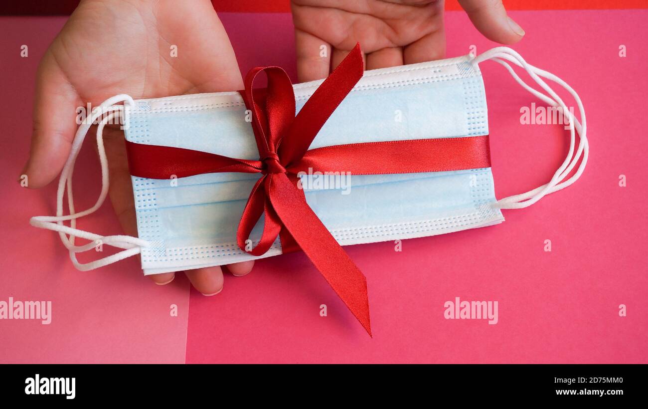 Surgical face mask with red ribbon as a present in hands on colorful ...