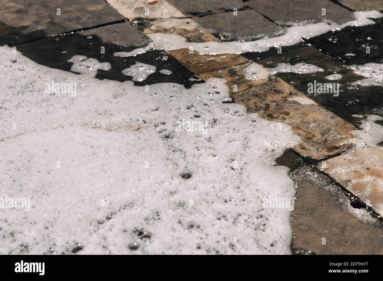 Foam streams on the asphalt from car wash, wet concrete texture ...