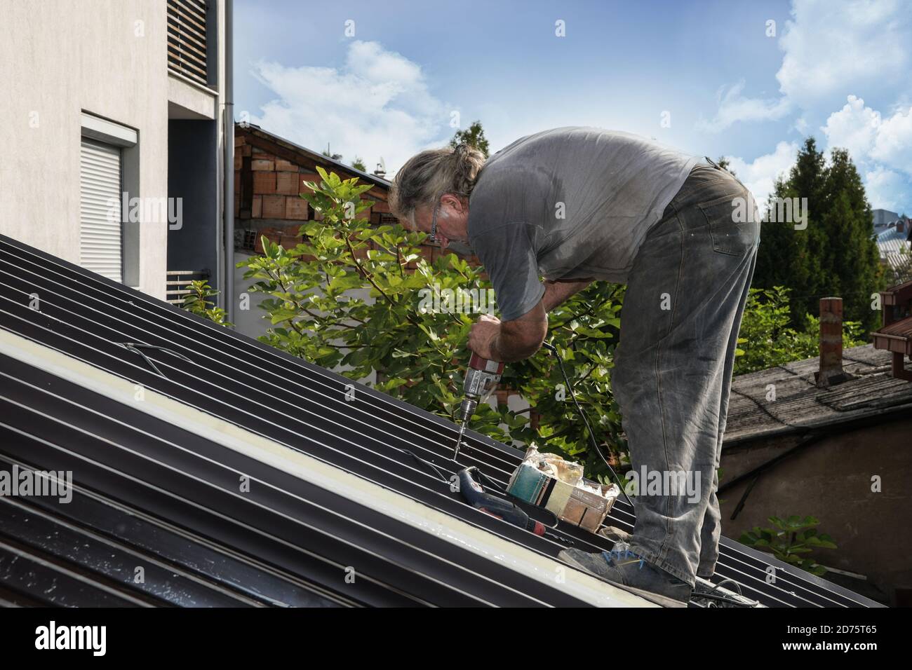 Repairing the roof of the house with screws drive tools. Worker roofer ...