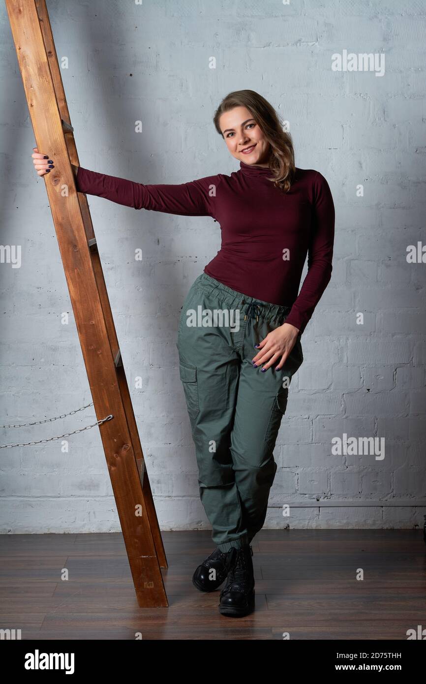 a girl with a wooden ladder stands near a white brick wall Stock Photo ...