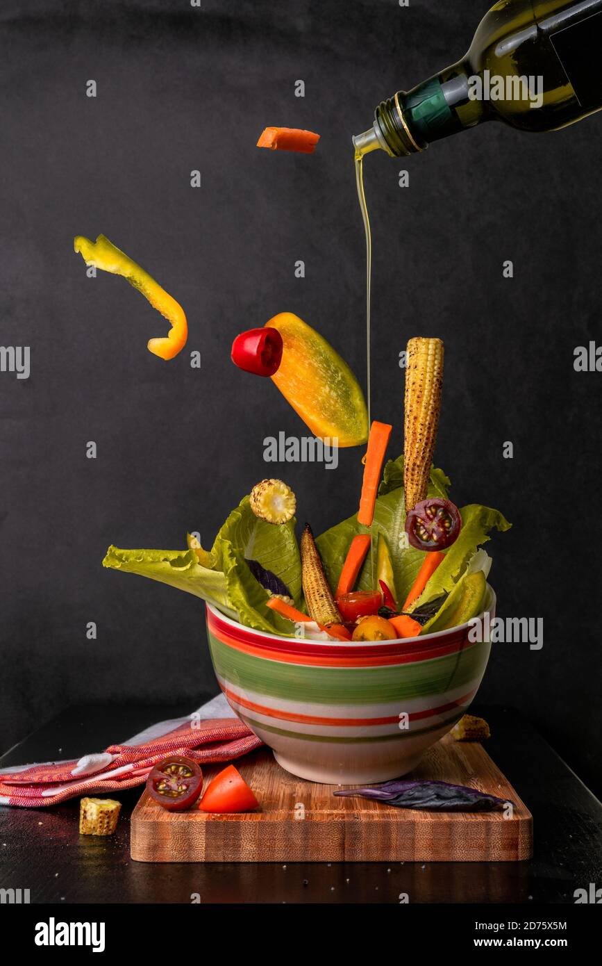Composition of flying vegetables falling into a bowl bathed in olive o ...