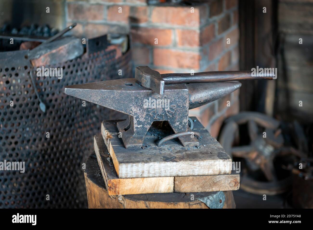 A vintage anvil and hammer on wood blocks in a forge or workshop. There's a steel hearth in the ...