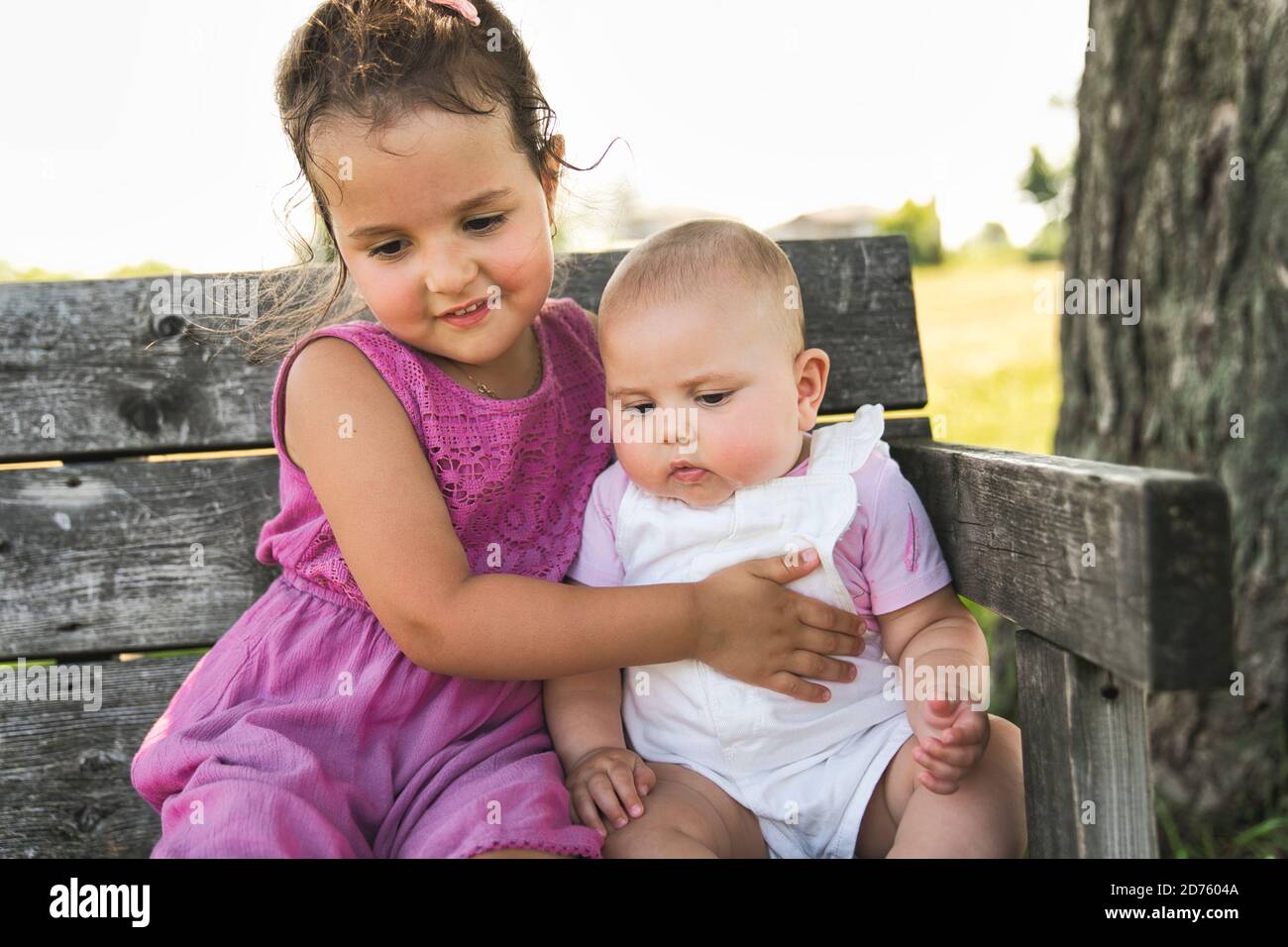 Happy adorable chubby baby girl sitting on a bench with her daughter ...