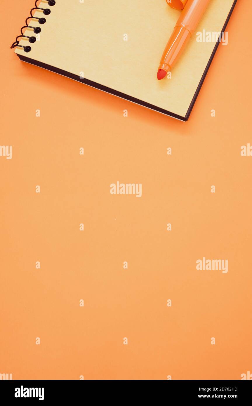 Vertical shot of a notebook and an orange marker on an orange surface ...