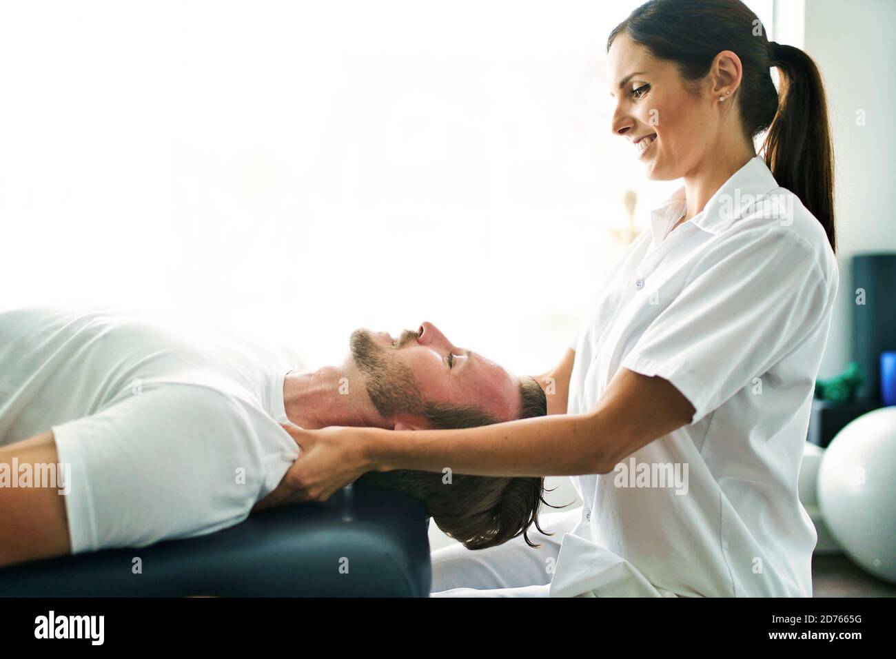 physiotherapist doing neck treatment with patient in bright office ...