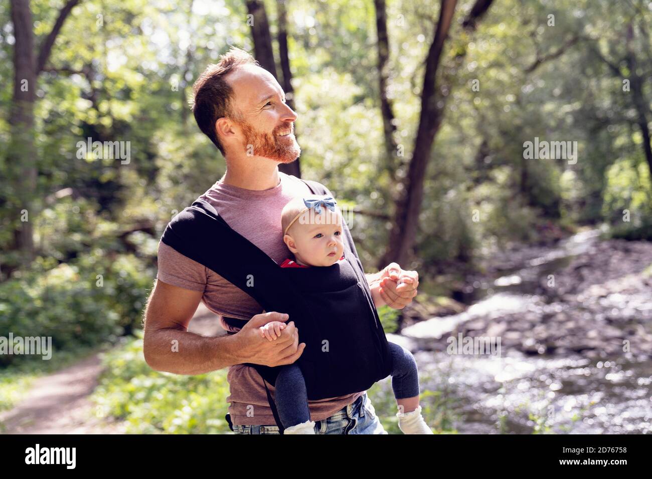 beautiful caring father holding her baby child in a sling walking on ...