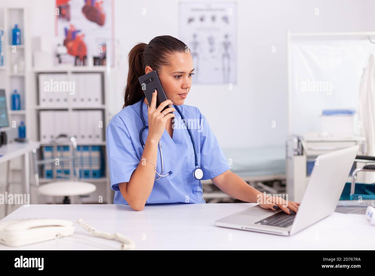 Medical practitioner using telephone and laptop in hospital office ...