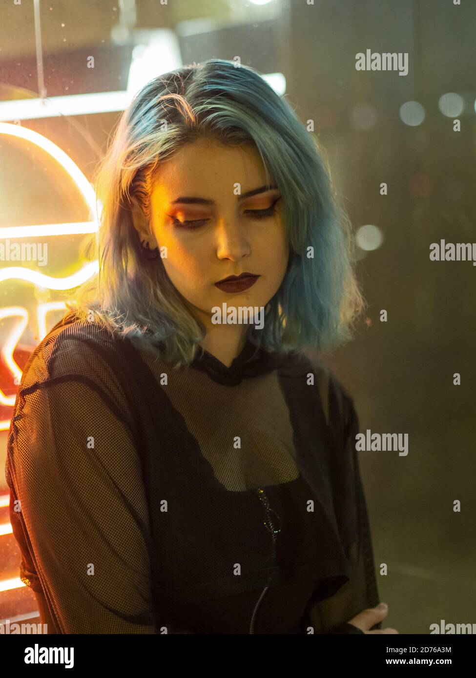 Shallow focus of a young female with blue hair posing near the led ...