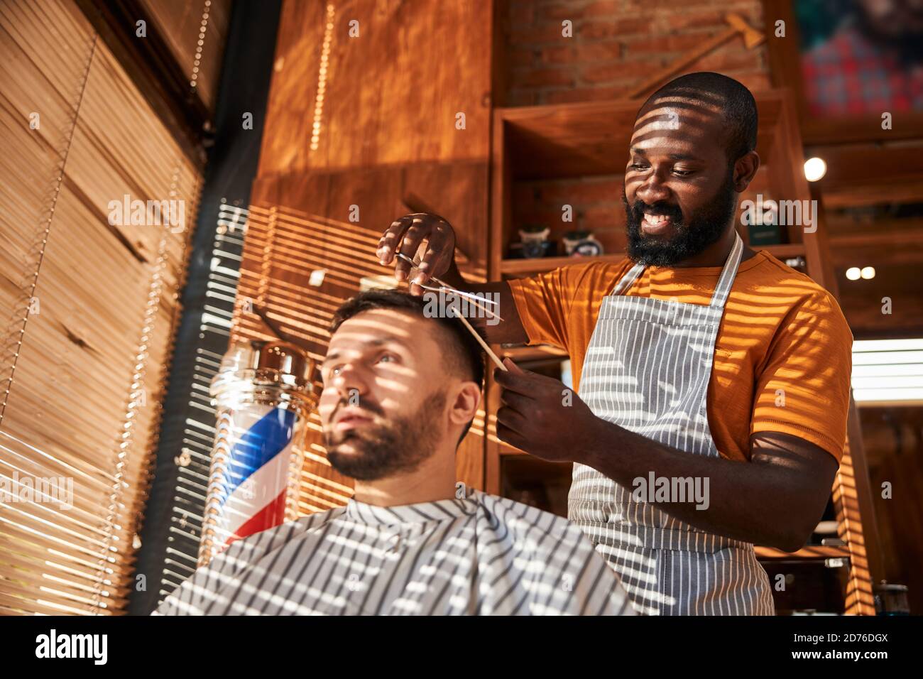 Smiling barber cutting client hair with scissors in barbershop Stock ...