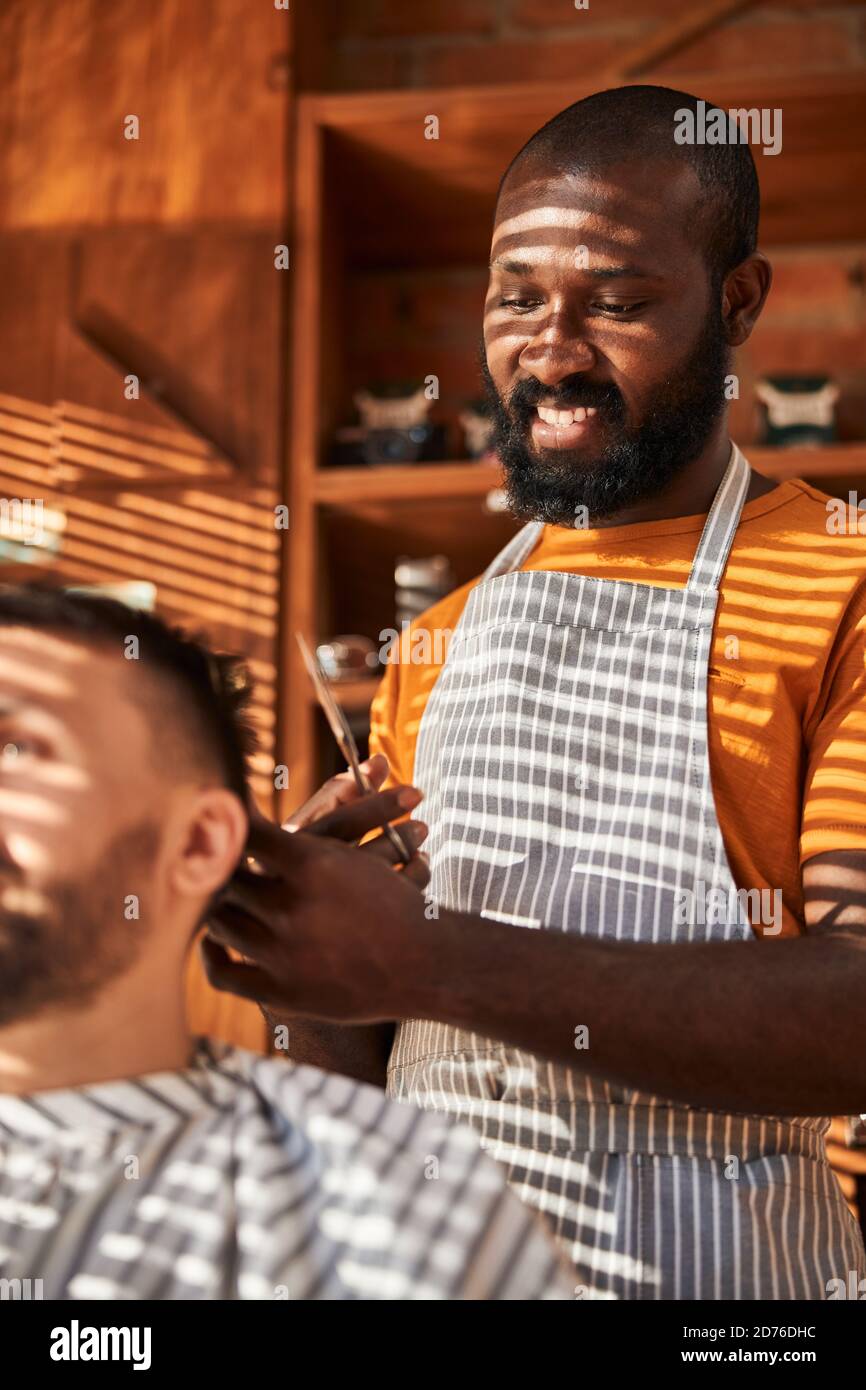 Smiling barber making haircut for client in barbershop Stock Photo - Alamy