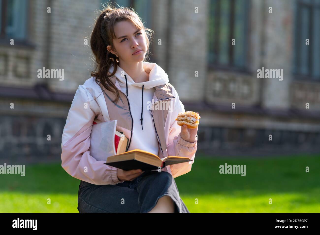 Young woman deep in thought sitting studying outdoors in evening ...