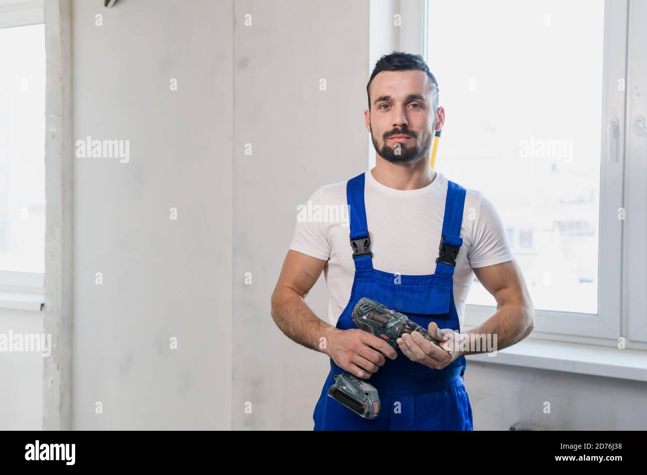 Builder in blue overalls posing with a drill Stock Photo - Alamy