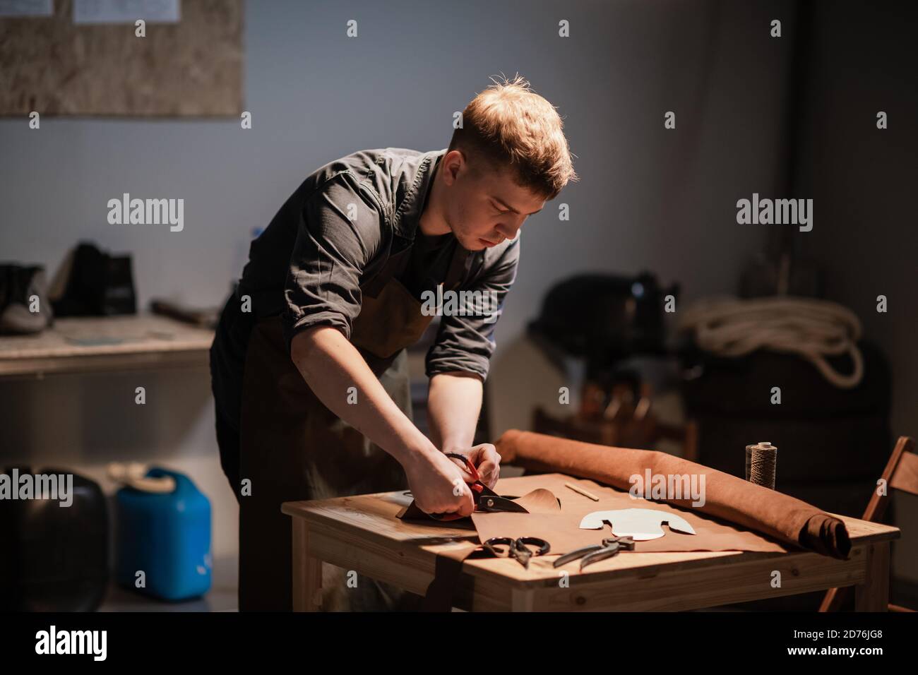 a young shoemaker in a Shoe shop makes shoes from leather with his own ...