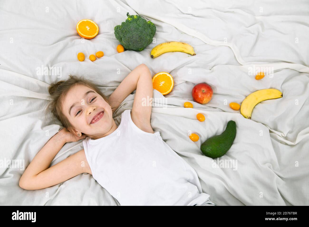 Cute little girl with fruits and vegetables on a light background ...