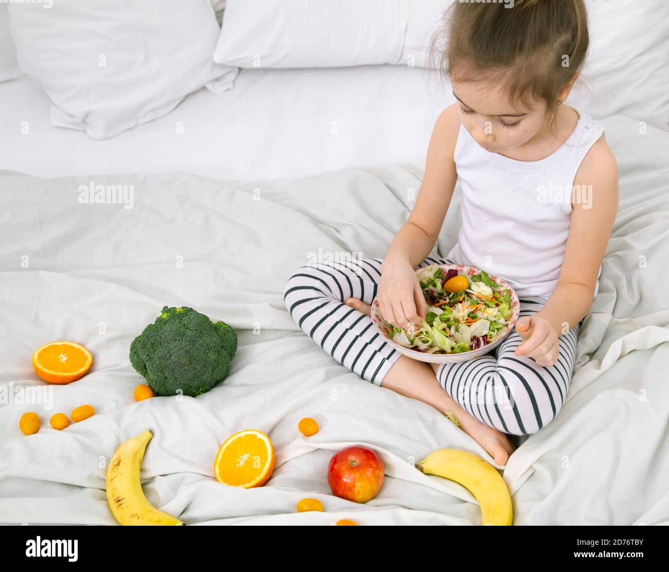 Cute little girl with fruits and vegetables on a light background ...