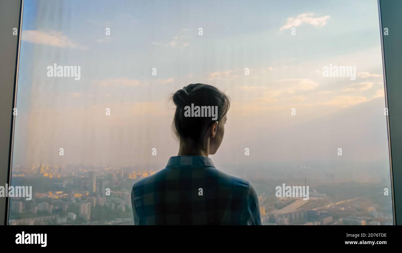 Back view of woman silhouette looking at cityscape through window of ...