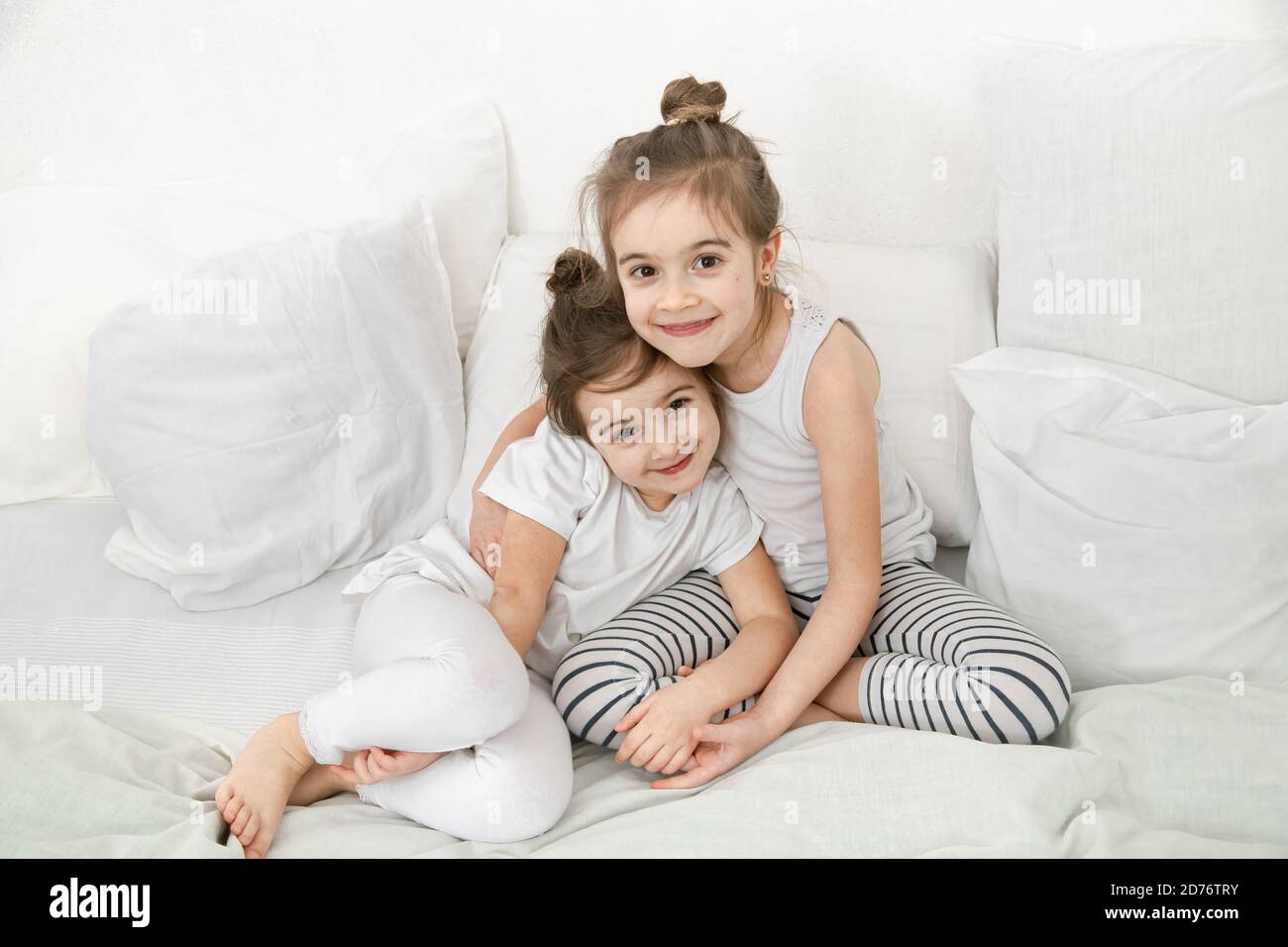 Two cute little sister girls are cuddling on the bed in the bedroom ...