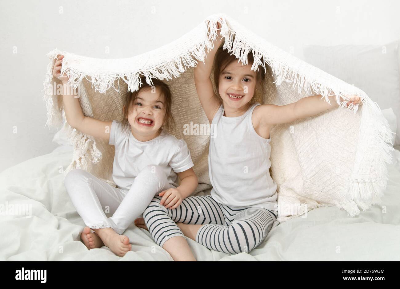 Two cute little sister girls are cuddling on the bed in the bedroom ...
