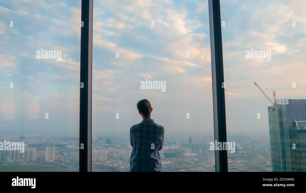 Back view of pensive woman silhouette looking at cityscape through ...