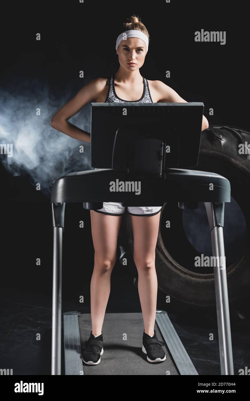 Young sportswoman standing on treadmill near tire in sports center with ...