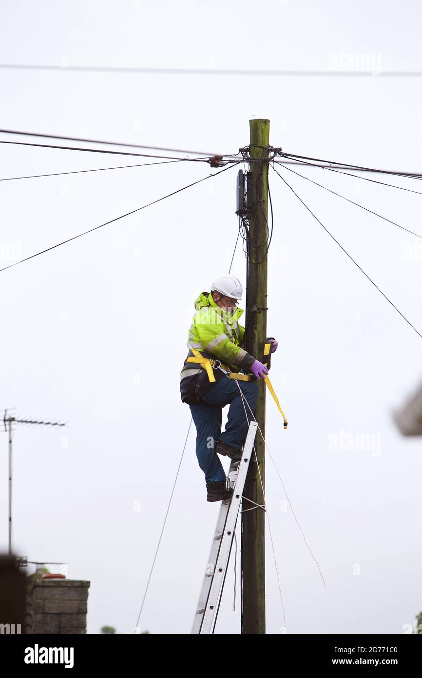 Open reach telecommunications engineer at work up a ladder, he is ...