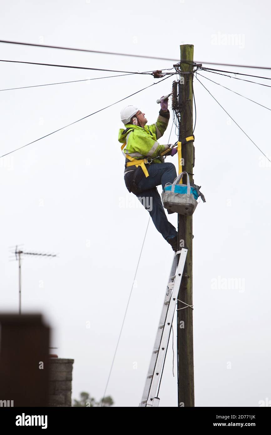 Open reach telecommunications engineer at work up a ladder, he is ...