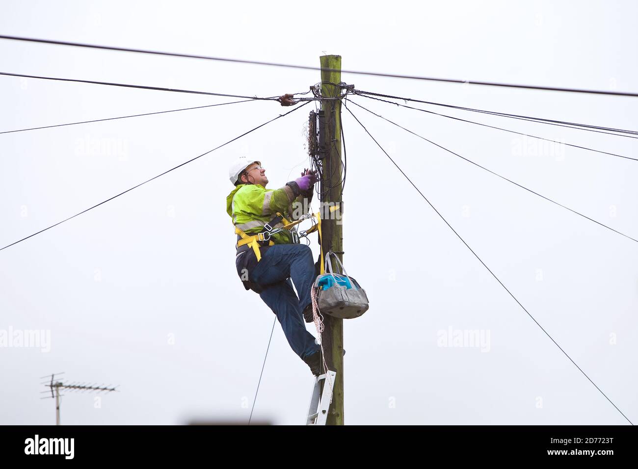 Open reach telecommunications engineer at work up a ladder, he is ...