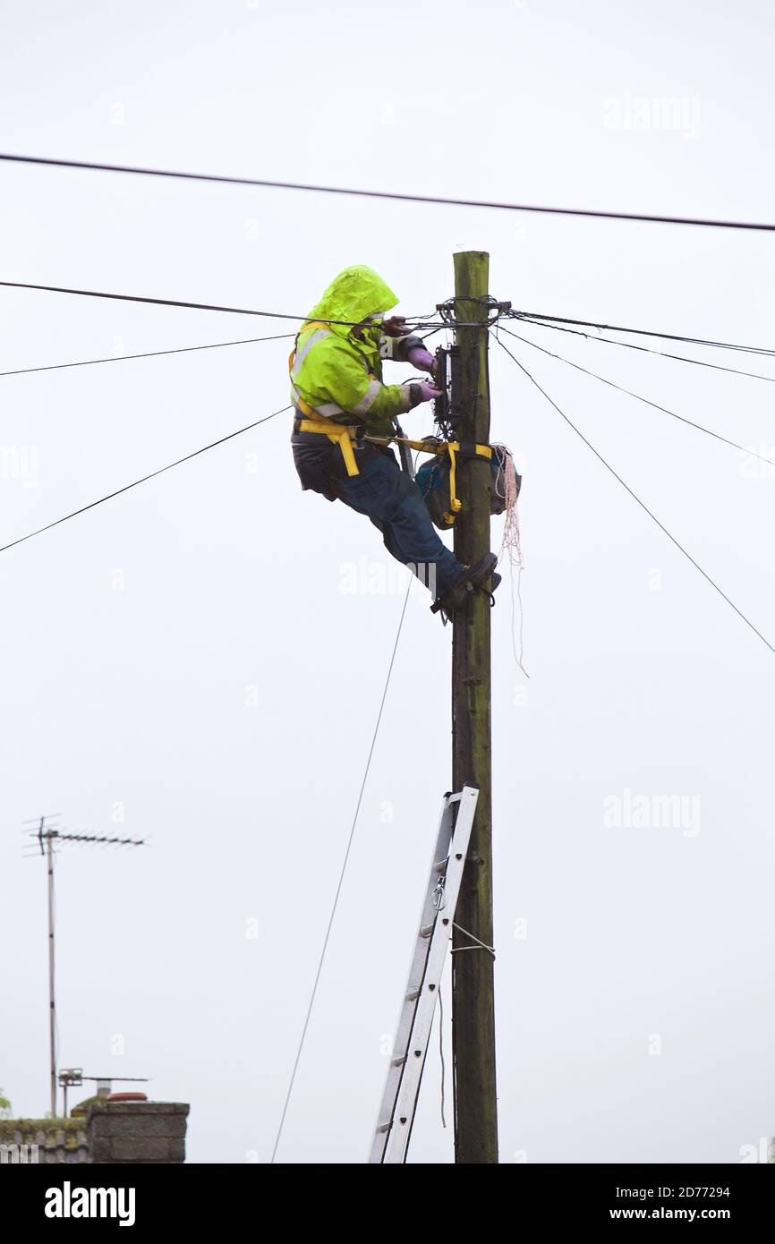 Open reach telecommunications engineer at work up a ladder, he is ...
