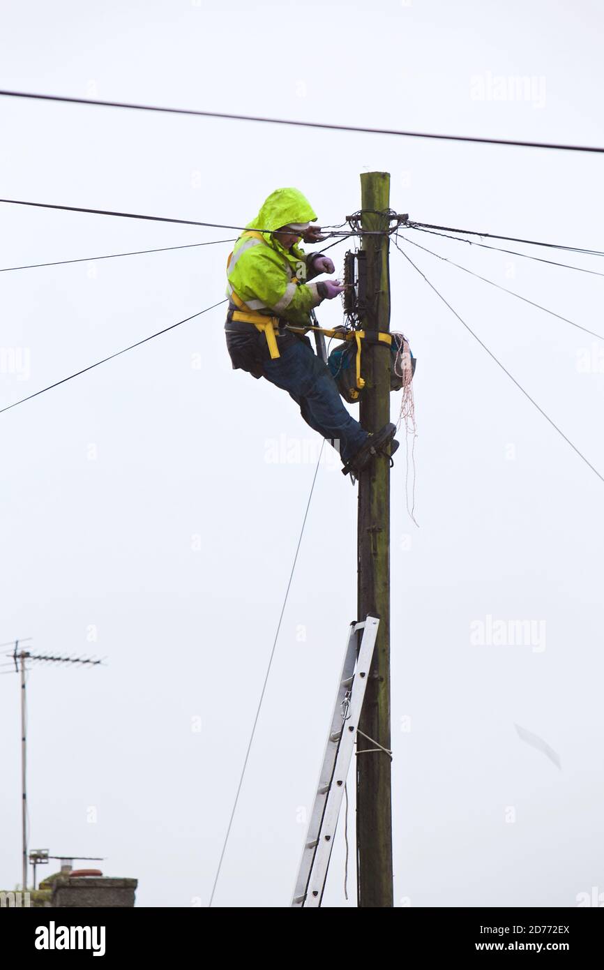 Open reach telecommunications engineer at work up a ladder, he is ...