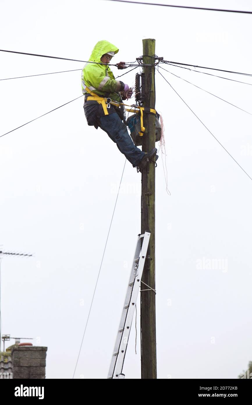 Open reach telecommunications engineer at work up a ladder, he is ...