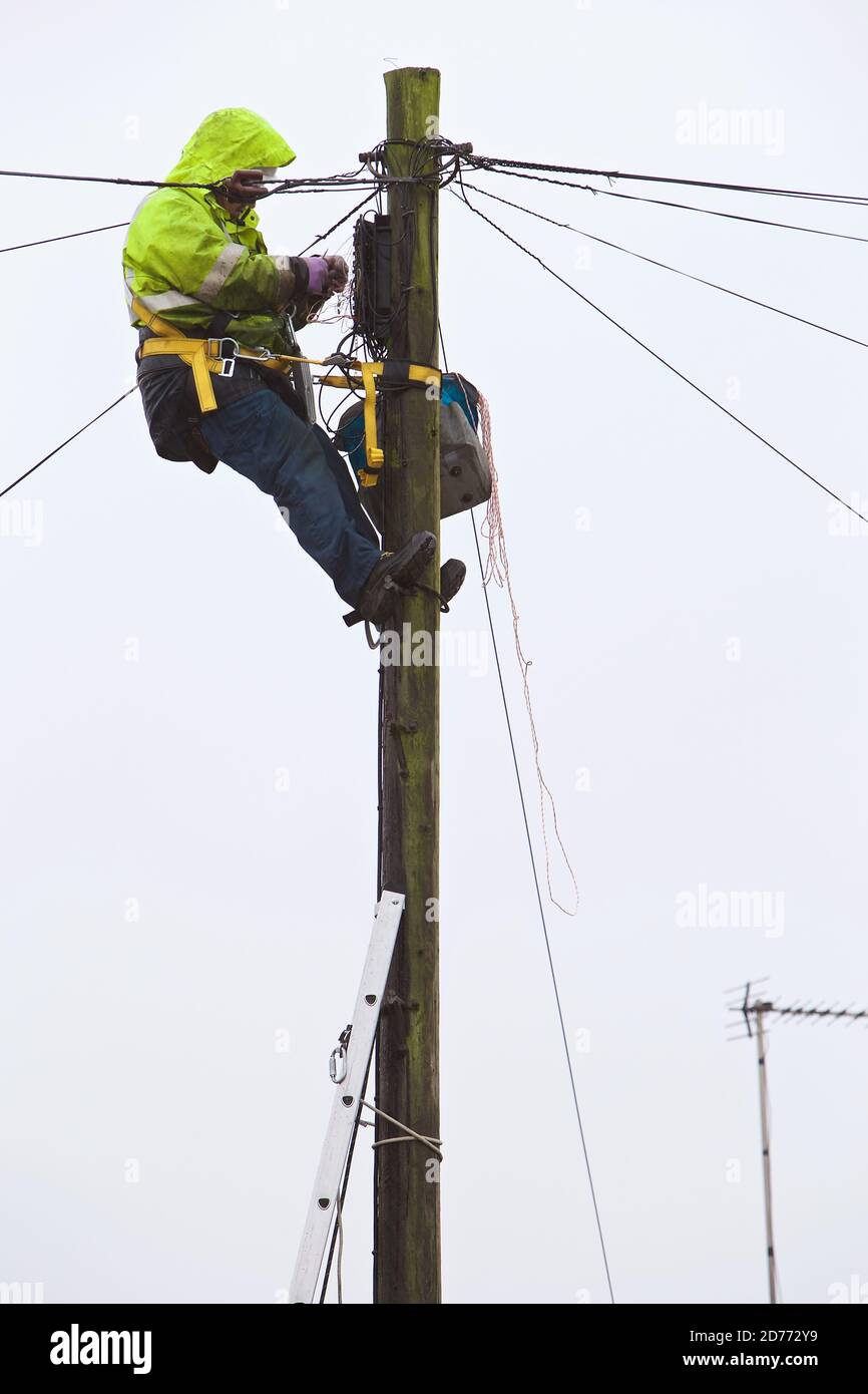 Open reach telecommunications engineer at work up a ladder, he is ...