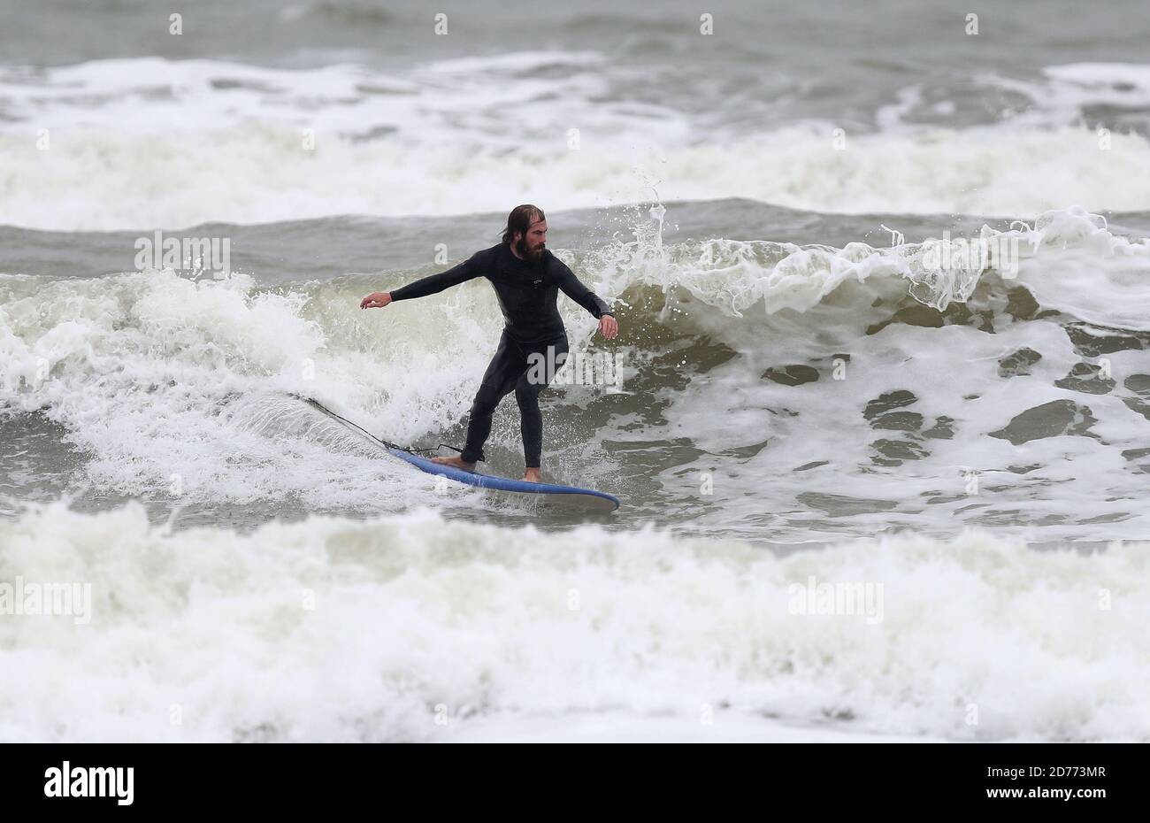 A surfer rides a wave in the sea at Bracklesham Bay in West Sussex ...